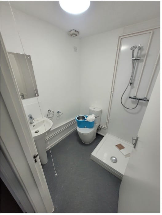 Small bathroom with a sink, toilet, and a shower area. A blue bucket ...