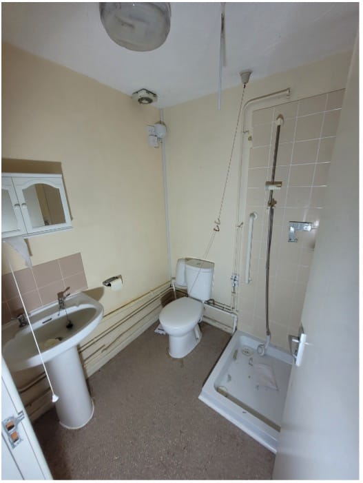 A small bathroom with a sink, toilet, and shower. Beige walls, a mirror ...